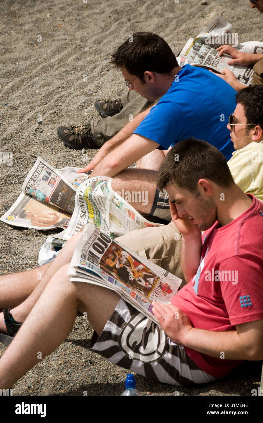 Four young men sitting on beach reading british english sunday tabloid ...