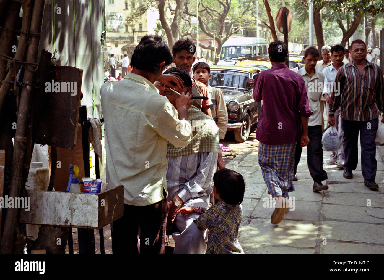 INDIA MUMBAI MAHARASHTRA Portable barber shop under a tree on a busy ...
