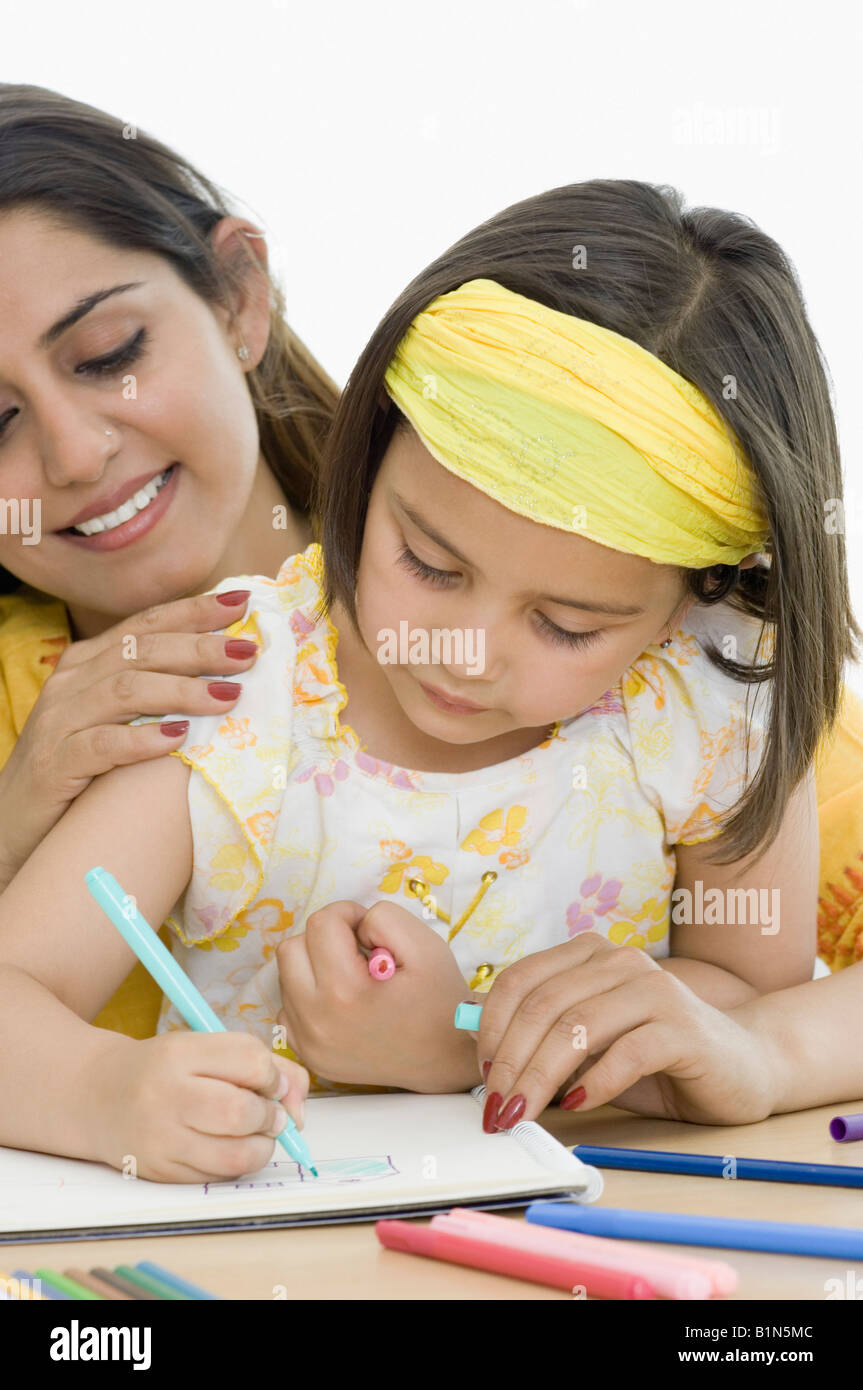 Close-up of a girl coloring on a coloring book with her mother behind ...
