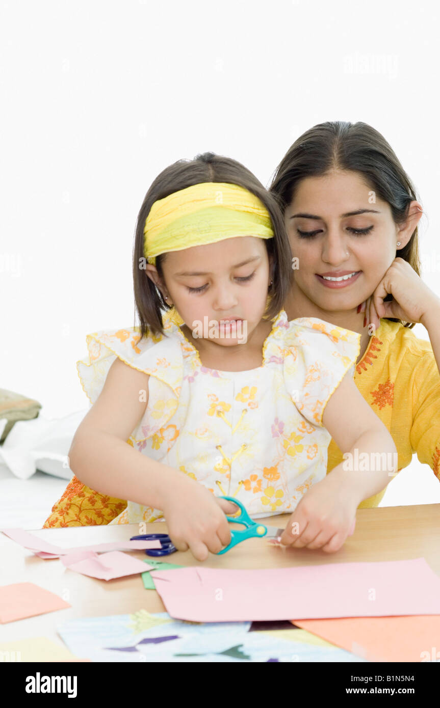 Girl cutting papers with scissors and her mother behind her Stock Photo ...