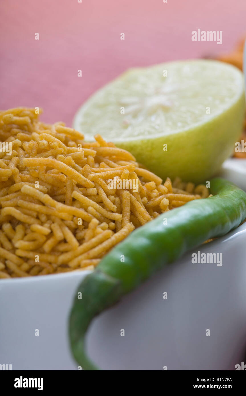 Close-up of a bowl of snacks with a slice of lemon and a green chili ...