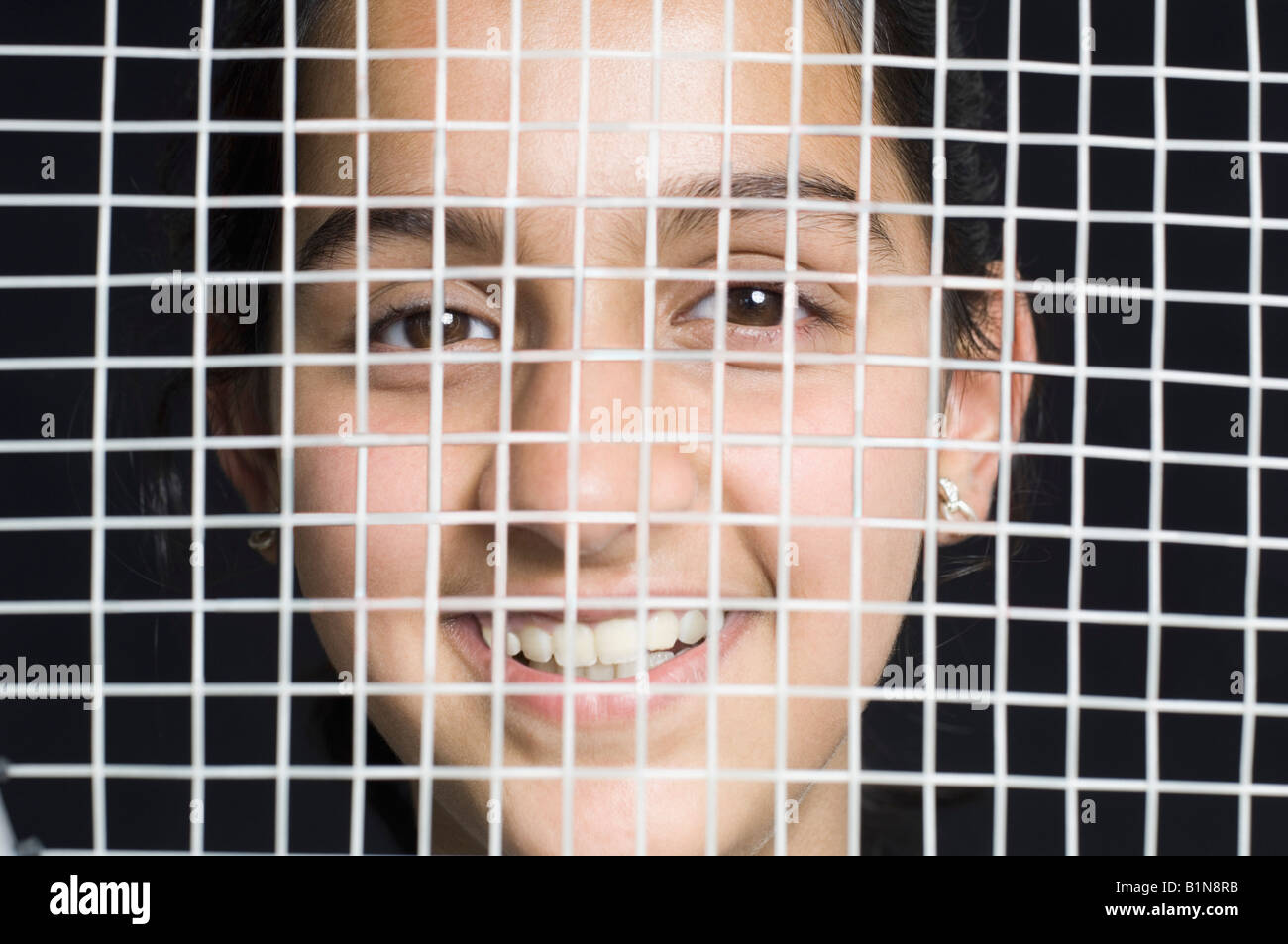 Portrait of a teenage girl hiding her face behind a net and smiling ...
