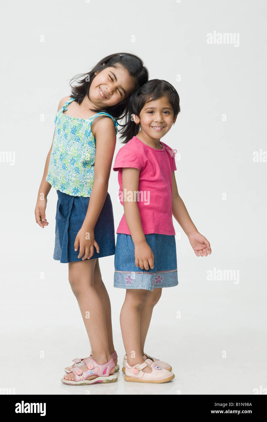 Portrait of two girls standing back to back and smiling Stock Photo - Alamy