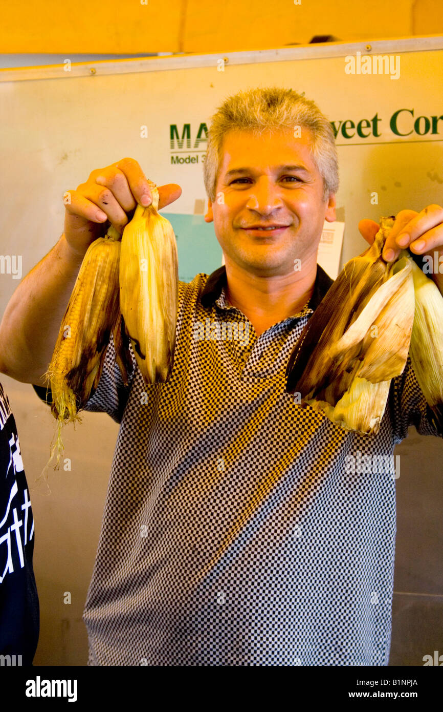 Man age 45 in food booth holding up freshly roasted corn on the cob ...