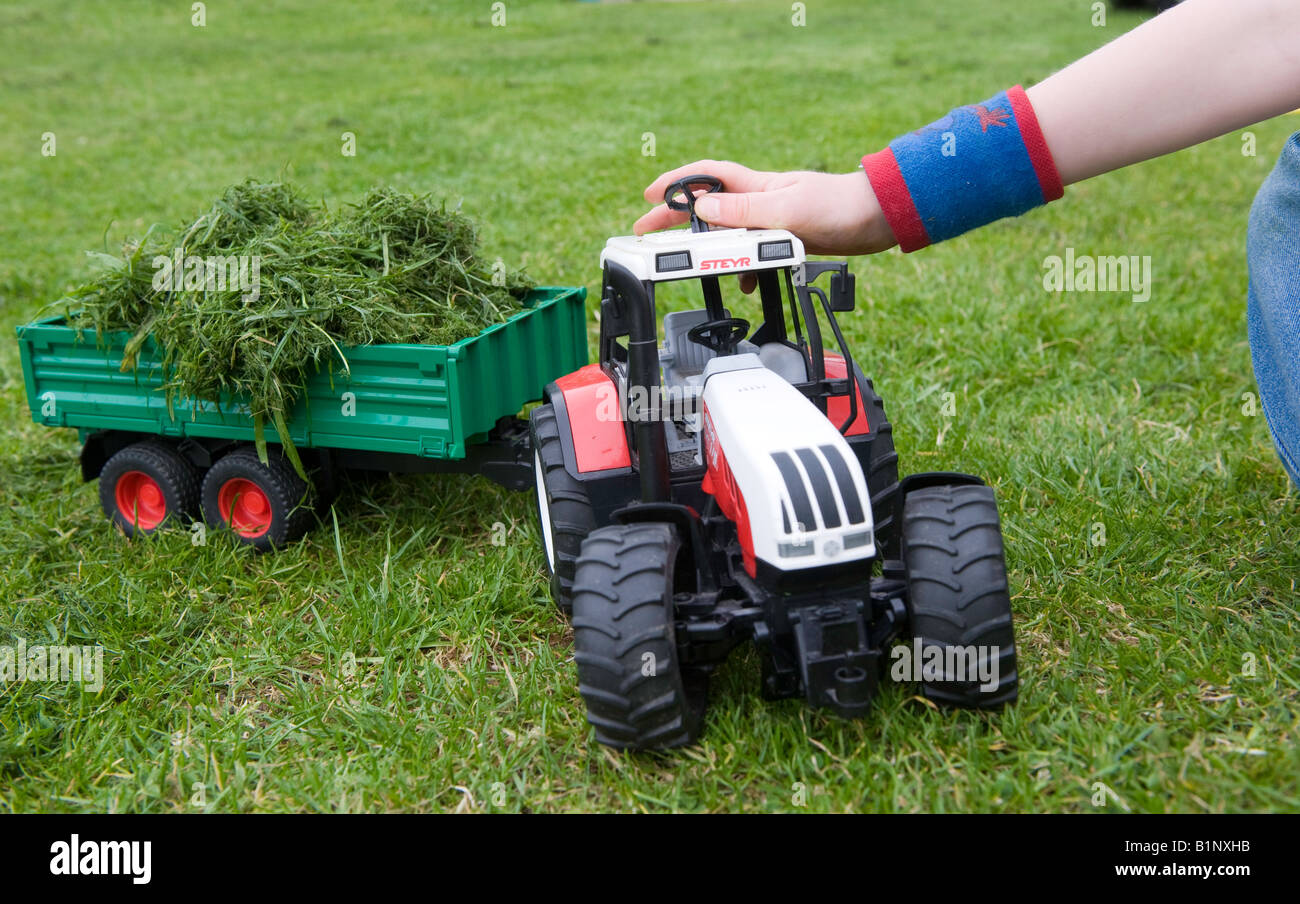 Young boy playing with tractor and trailer in garden pretending to make ...