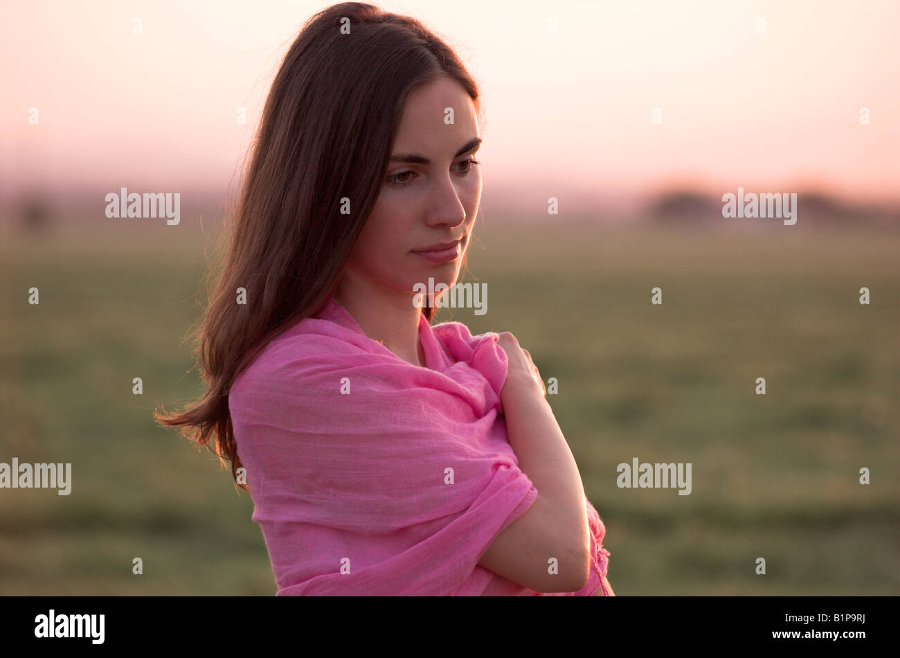 Portrait of a beautiful young woman standing outdoors looking down ...