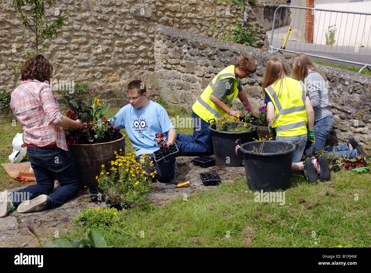 High school students planting flowers in round wooden pots at a ...
