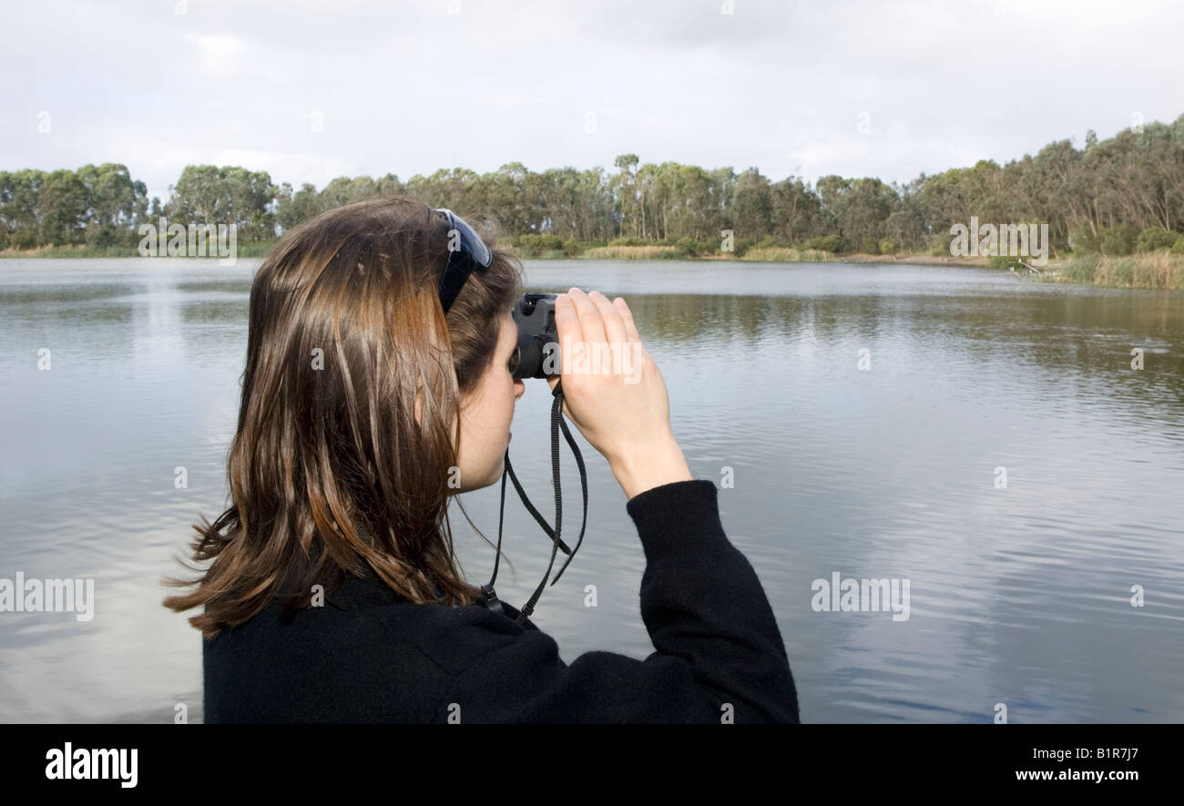 A woman with binoculars birdwatching at a lake. With main focus on the ...
