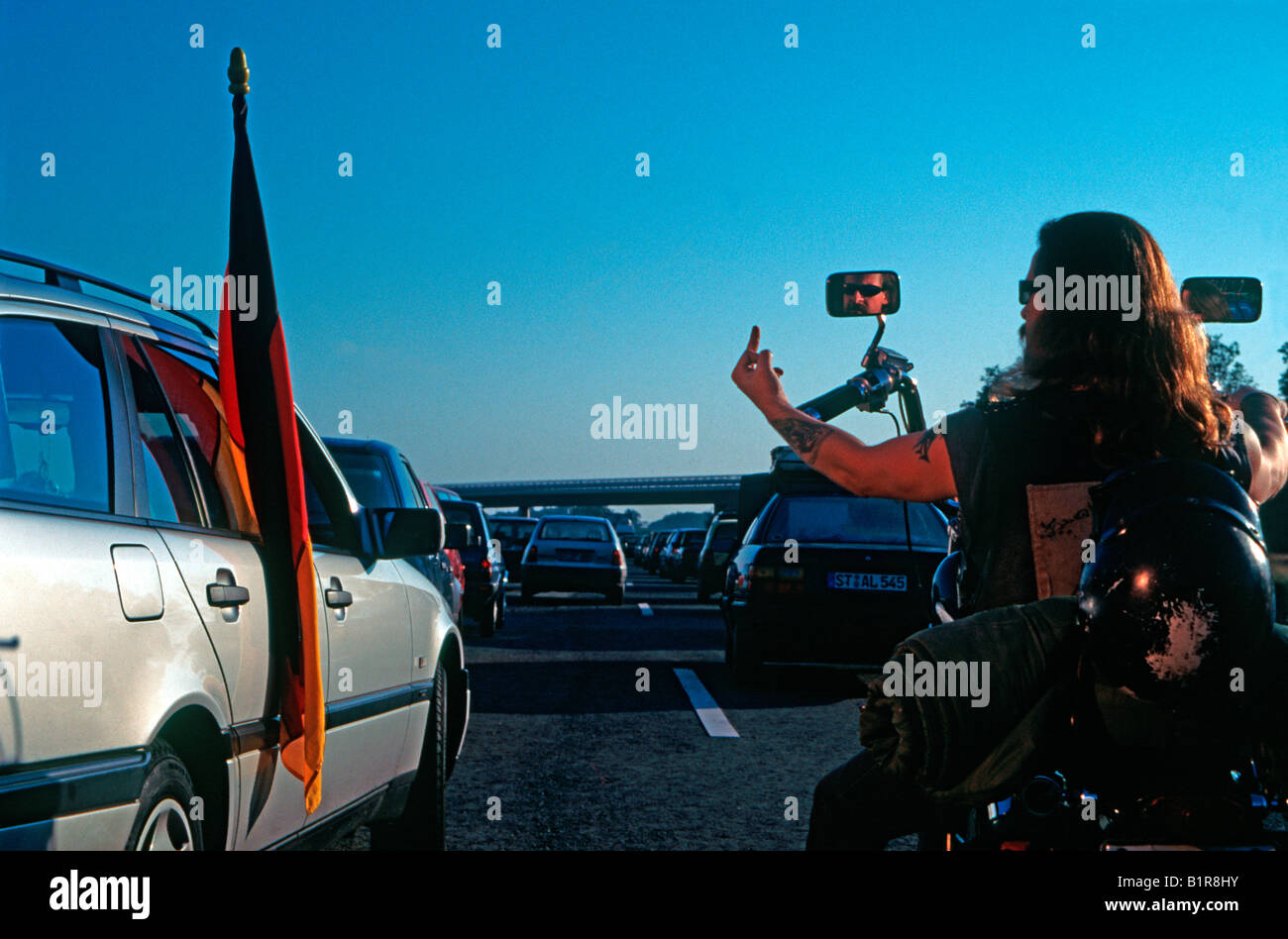 biker giving finger to cars trapped in traffic jam a German flag is ...