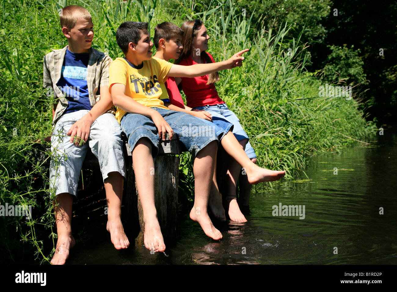 kids sitting on a landing stage beside a stream Stock Photo - Alamy