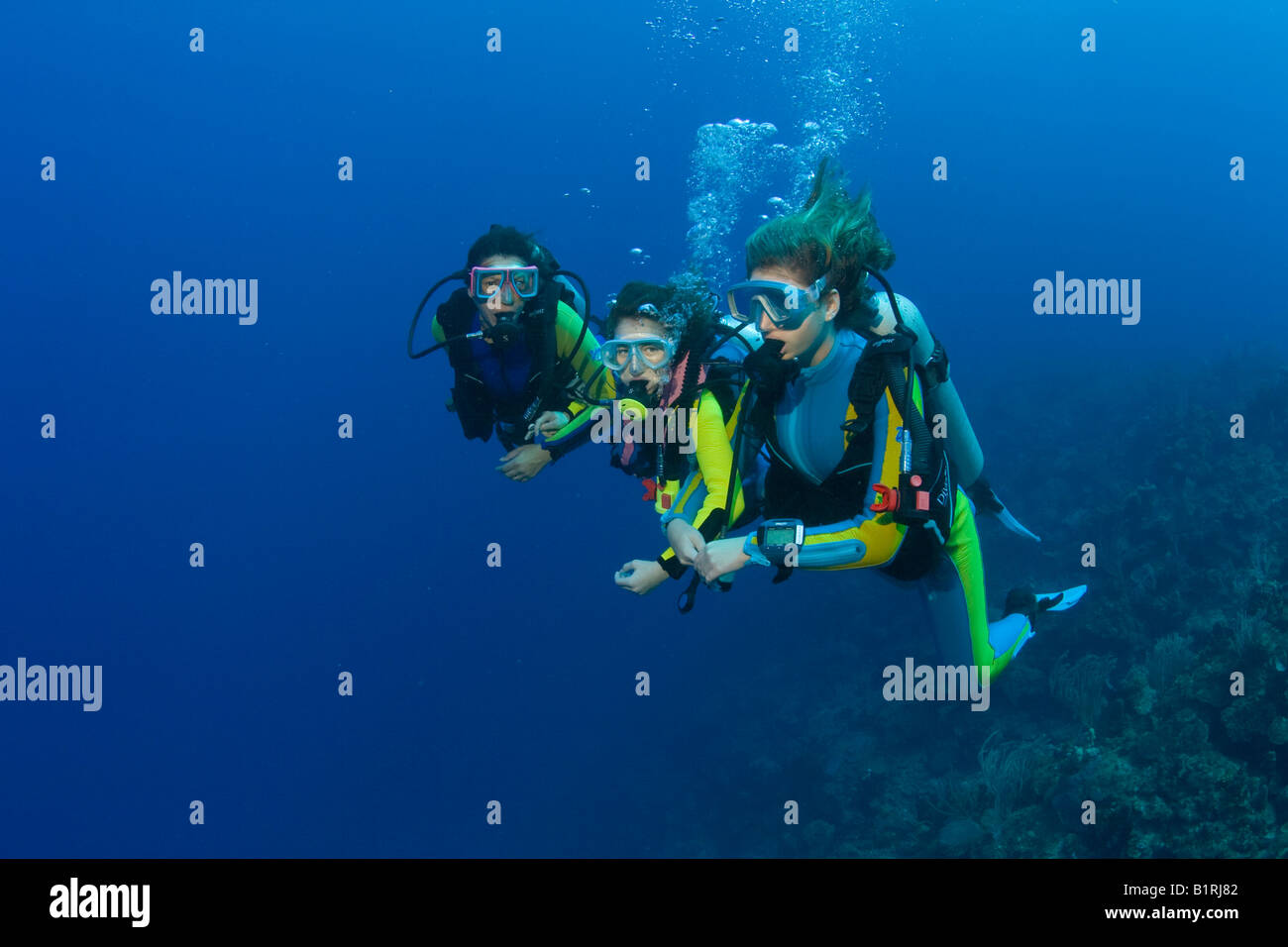 Three scuba divers, mother and daughters, diving over a coral reef ...