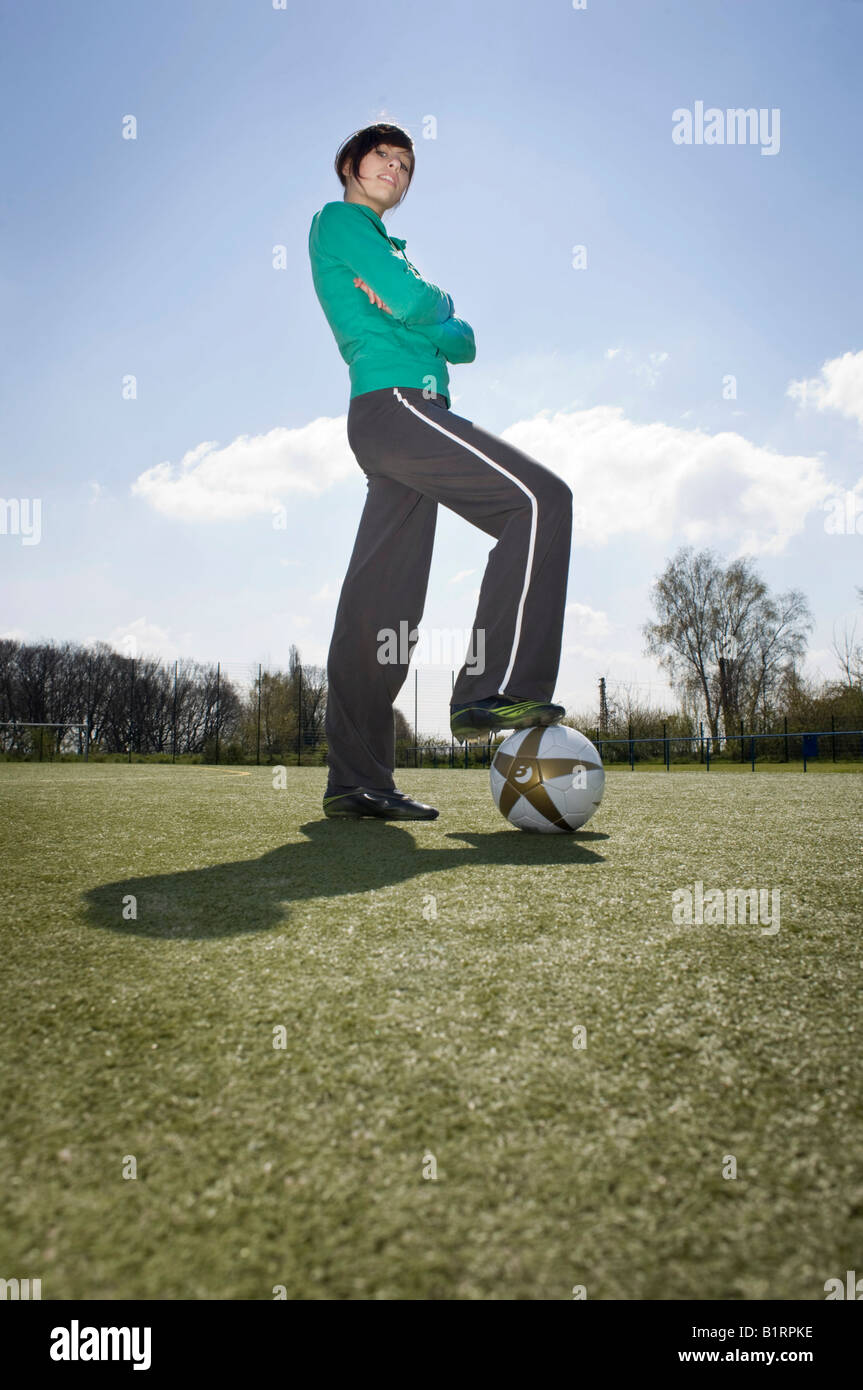 Young woman on a sports field with crossed arms and a football under ...