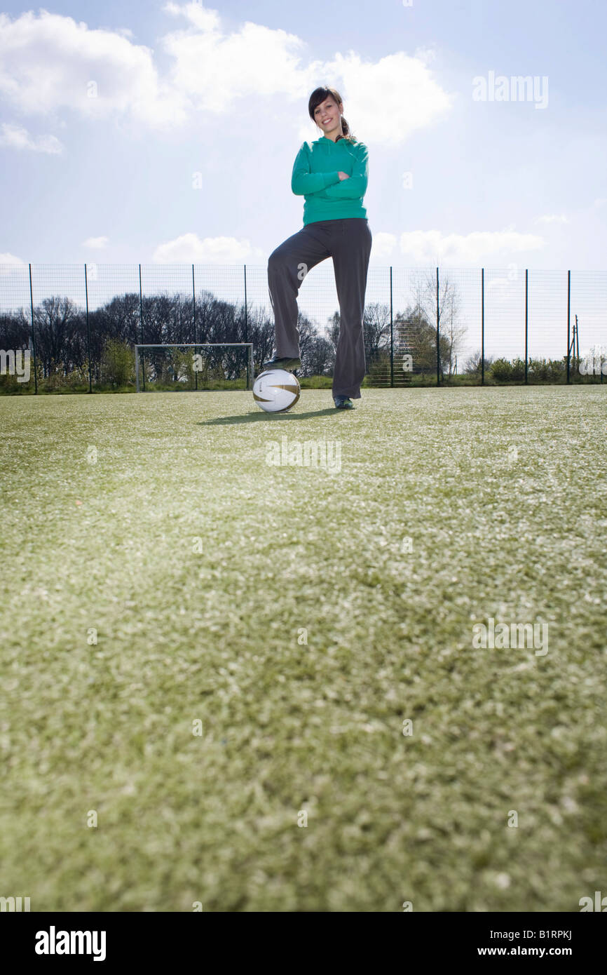 Young woman standing on a sports field with a football under her foot ...