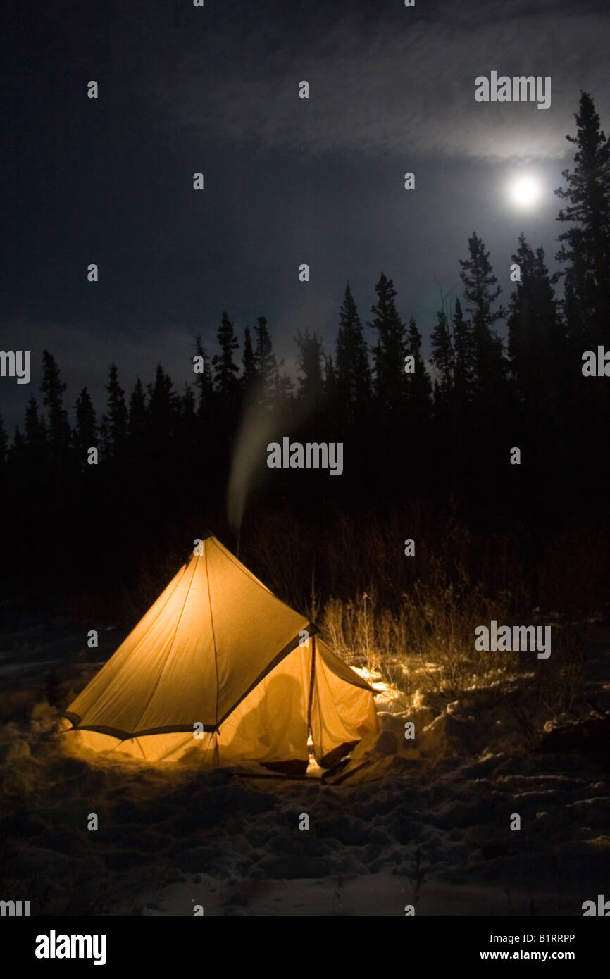 Illuminated tent with smoke coming out of a stove pipe, moon, Yukon ...