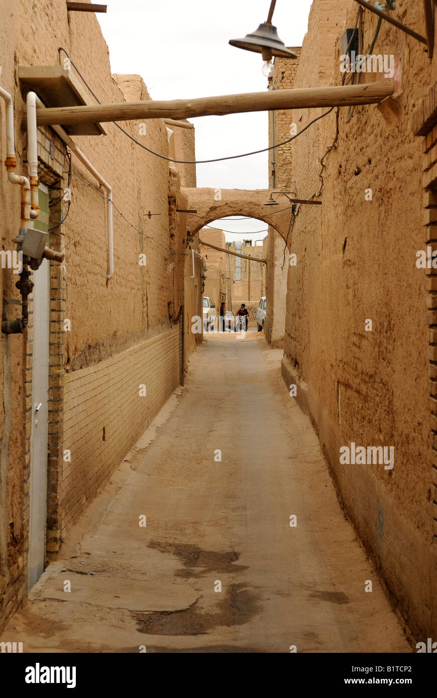 Long alleyway in the old sector of Yazd where two youths talk to each ...