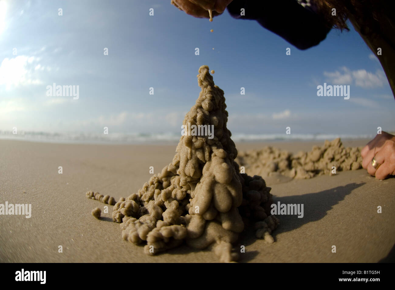 Hand dripping wet sand onto a sand castle on the beach Stock Photo - Alamy