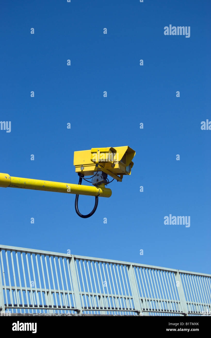 seen against a blue sky, a yellow cctv camera on a yellow arm watches ...