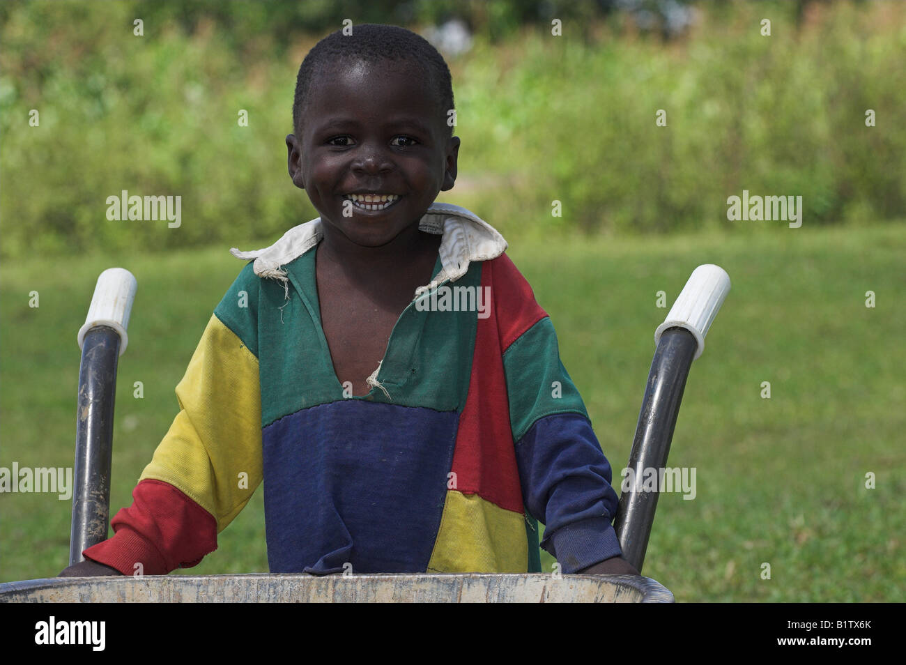 Young African boy wearing checked rugby shirt pushing wheelbarrow Kenya ...