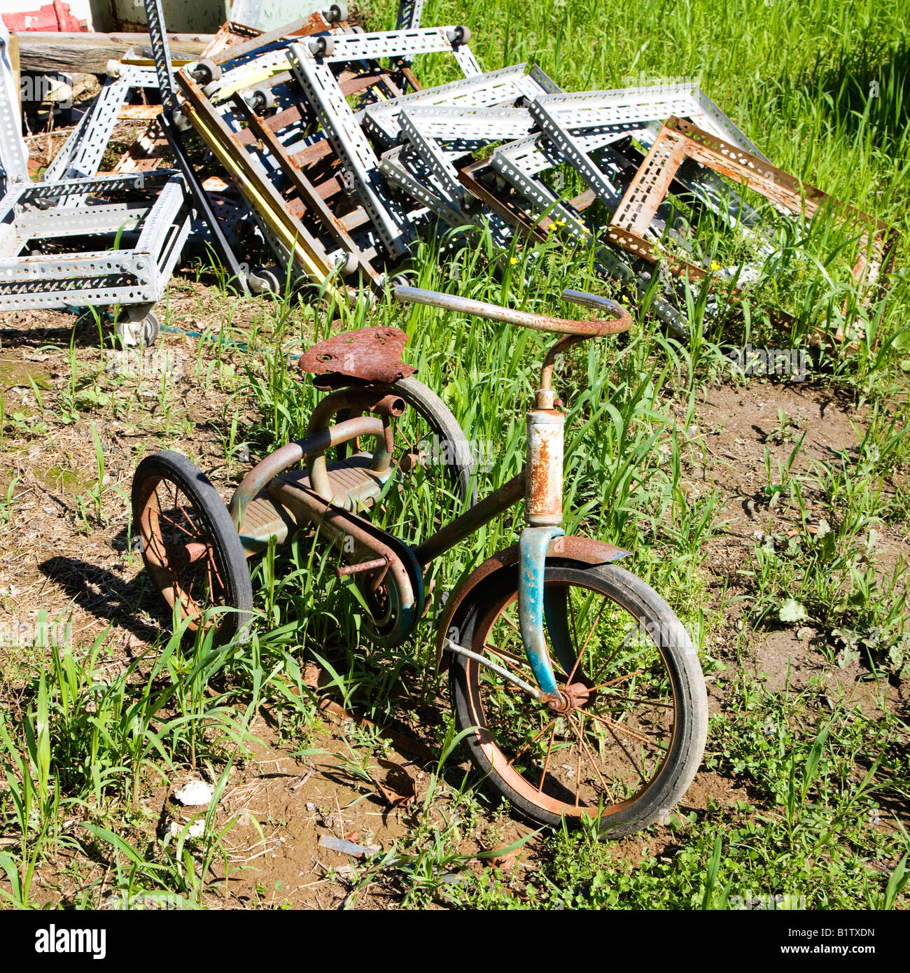 Old abandoned tricycle in grassy field next to junk pile Stock Photo ...