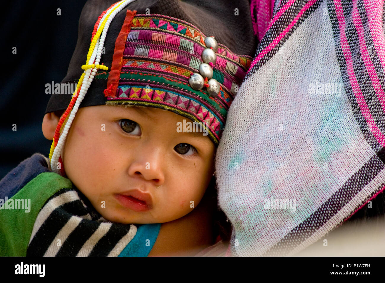 A baby Akha hilltribe child rests on his mother's shoulder in the ...