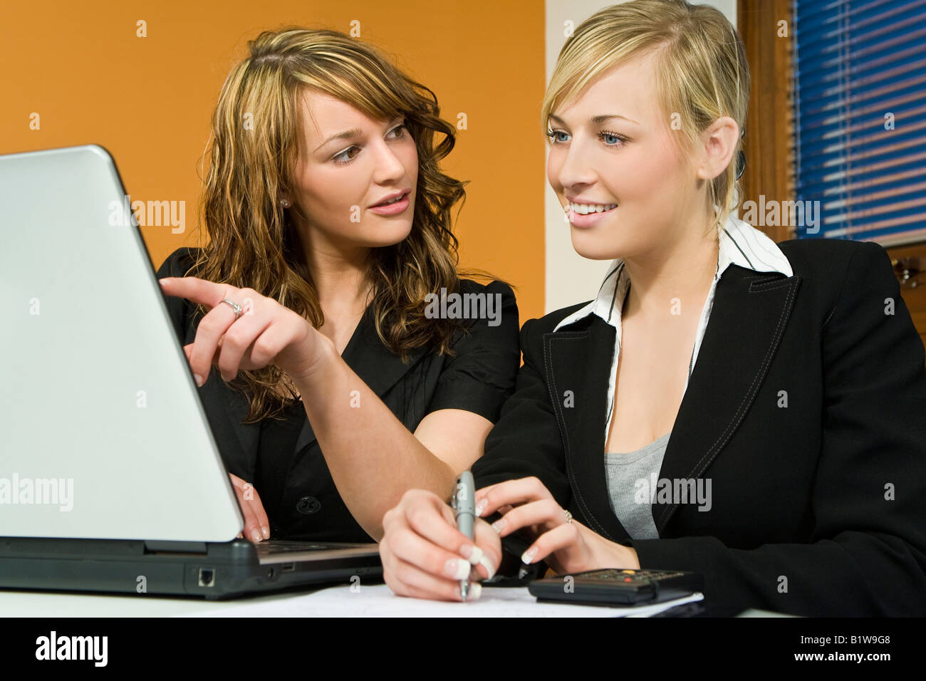 Two attractive young female executives working together on a laptop ...