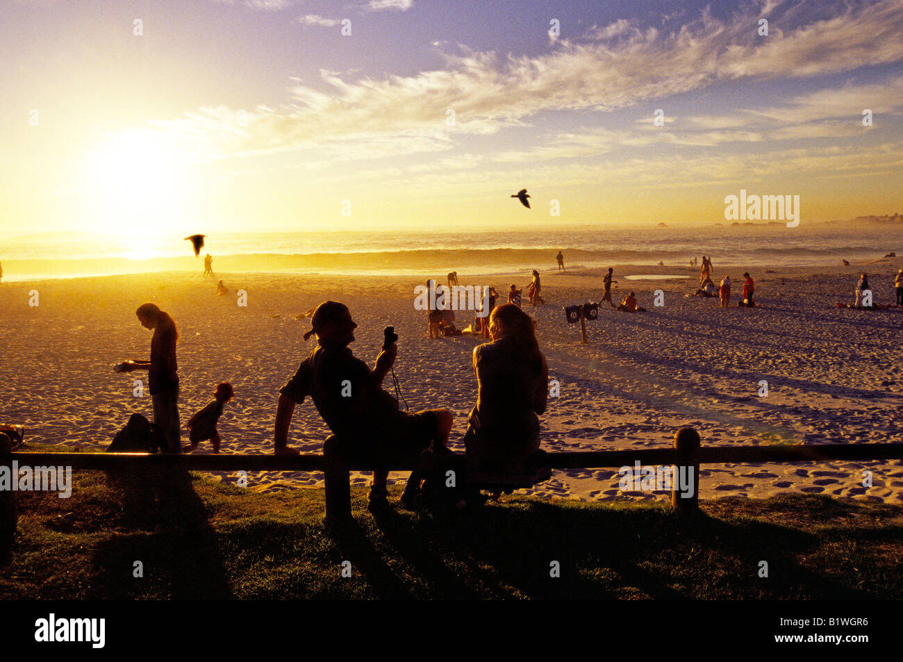 Tourists taking pictures of each other on Camps Bay beach at sunset ...