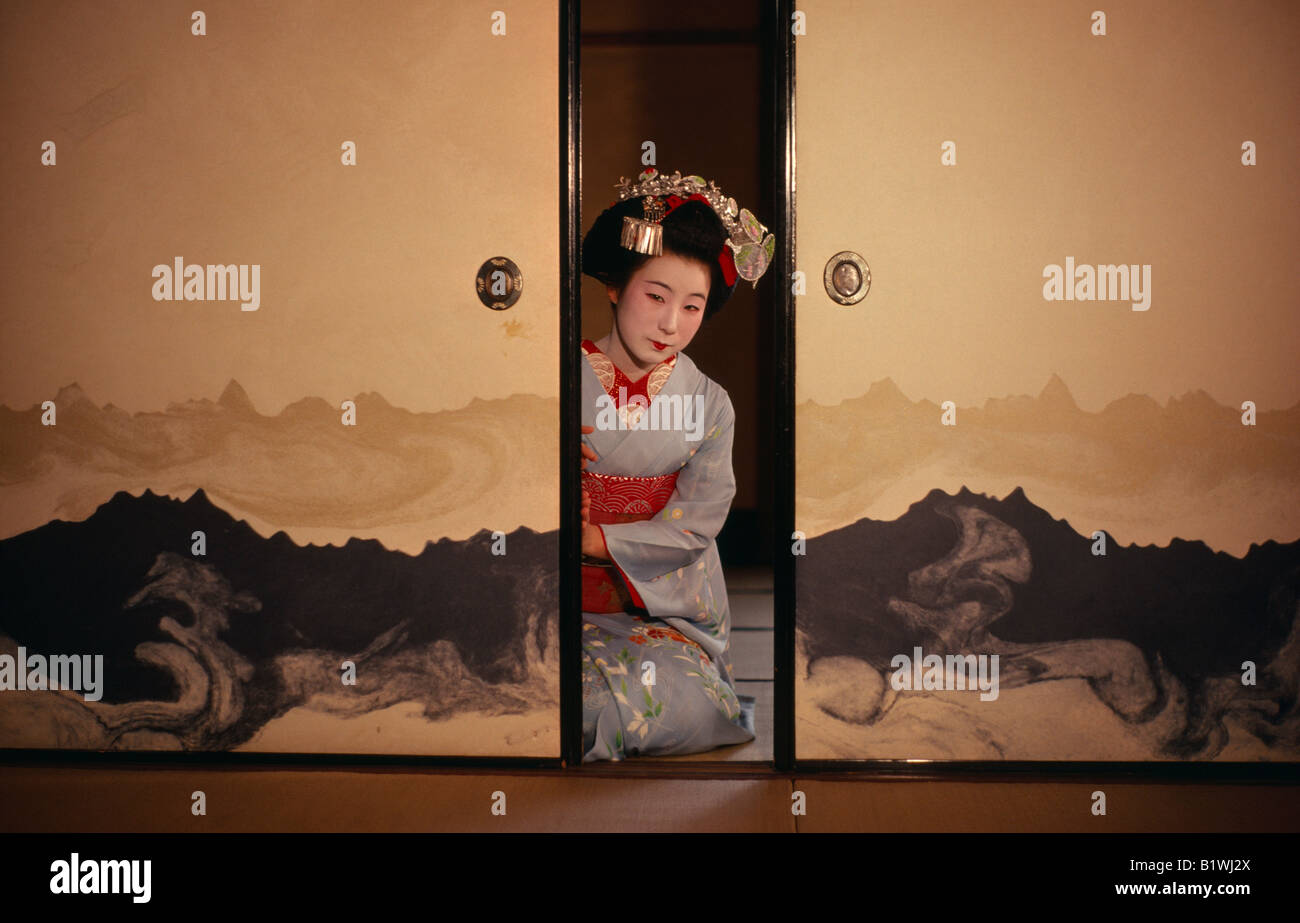 JAPAN Maiko or trainee Geisha wearing kimono and full make-up kneeling ...