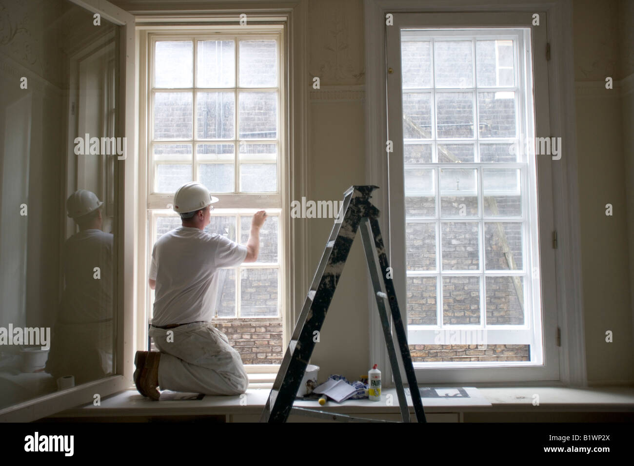 A decorator finishes painting the windowframes of a building interior ...