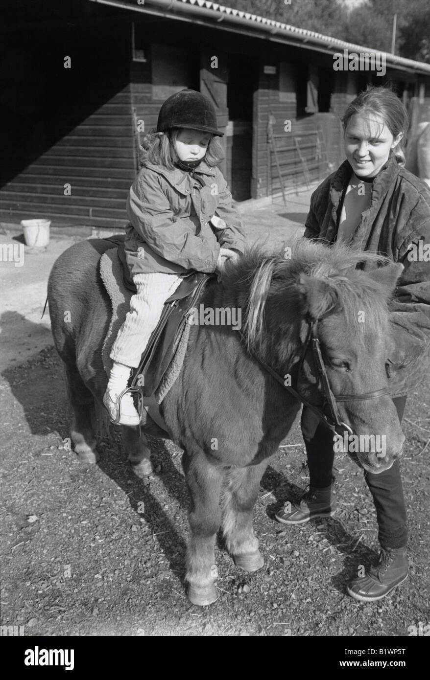 Apprehensive little girl astride a pony for her first ride being held ...