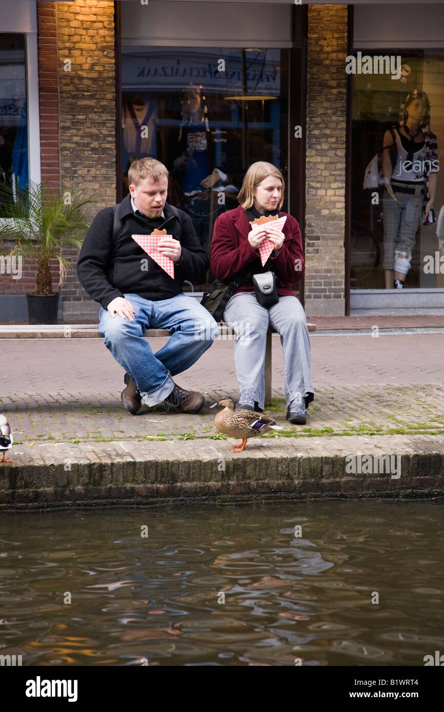 Couple sitting and eating Dutch waffle while watching a duck, by the ...