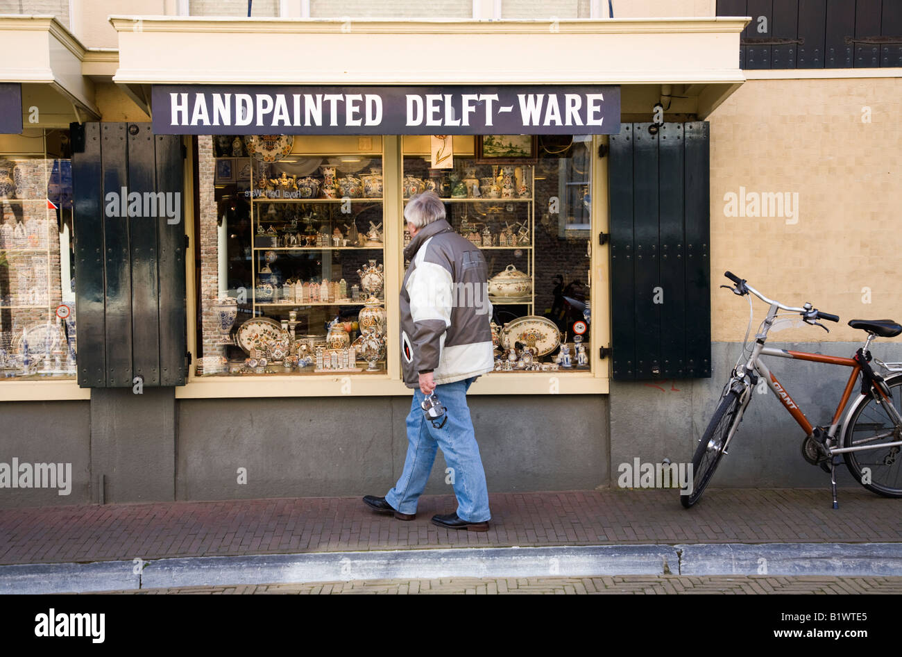 Passer by looks at Royal Delftware pottery on display in a shop window ...