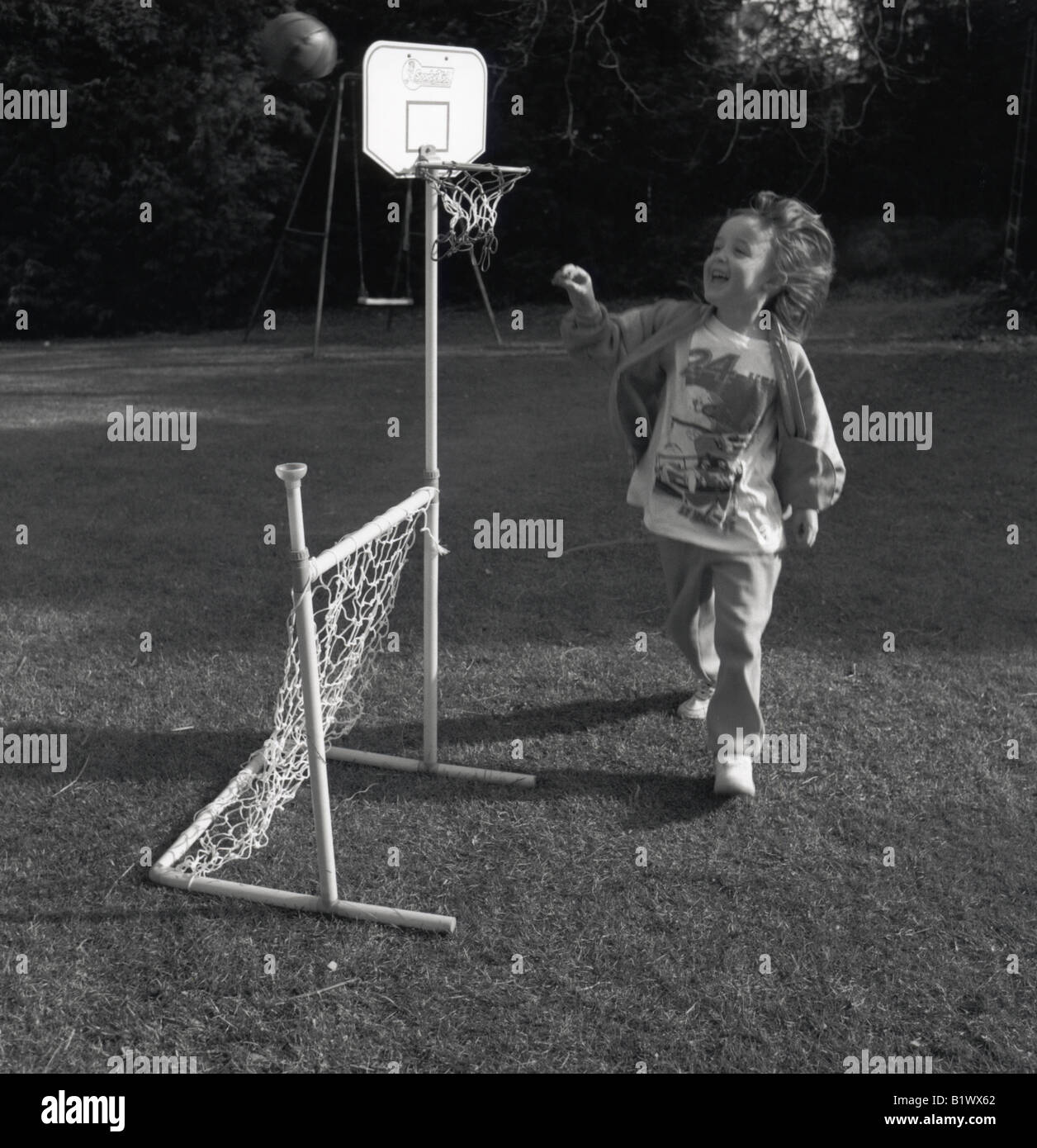 Laughing little girl running and throwing a ball into a toy basketball ...