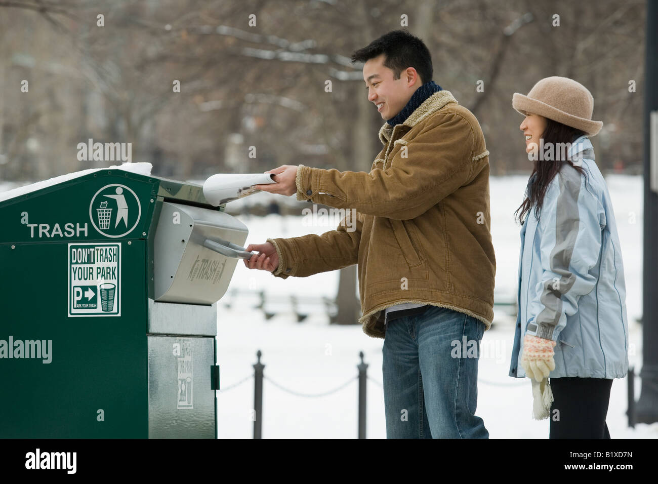 Young man throwing garbage into a garbage bin with a young woman ...