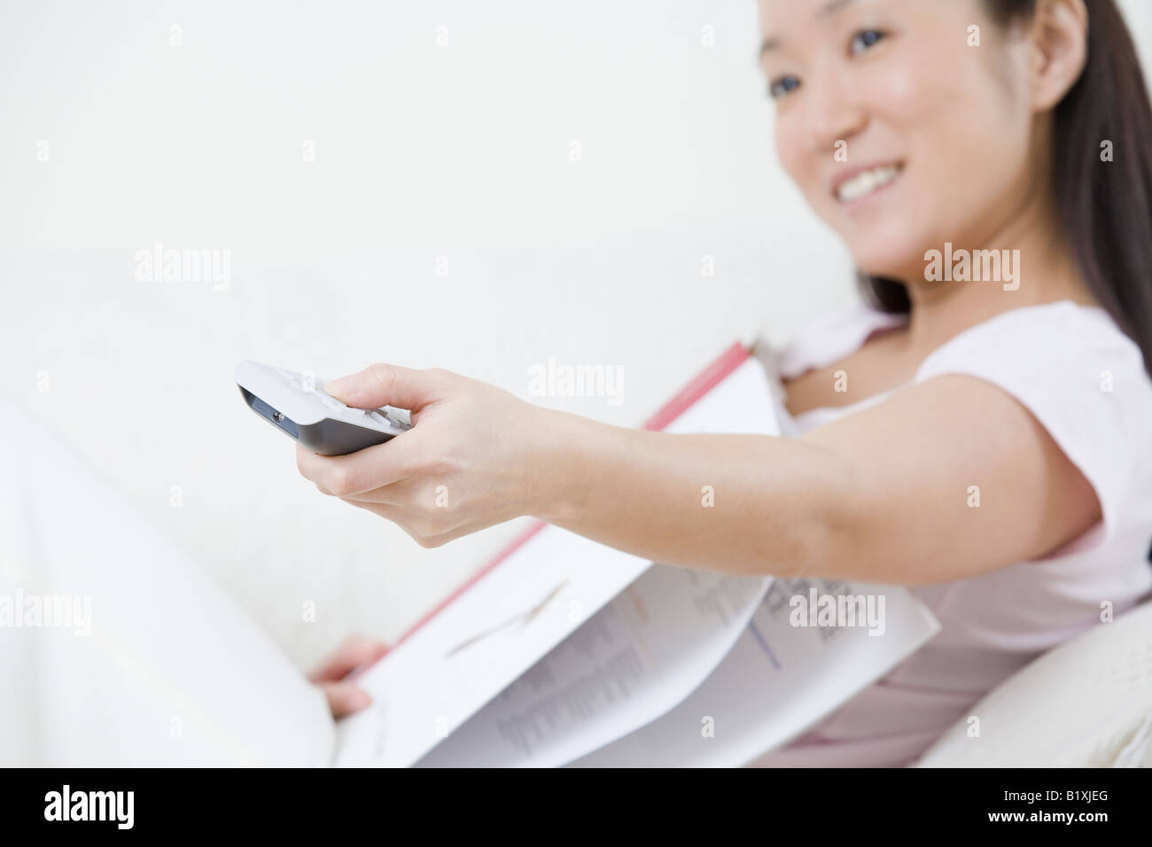 Young woman using a TV remote control Stock Photo - Alamy