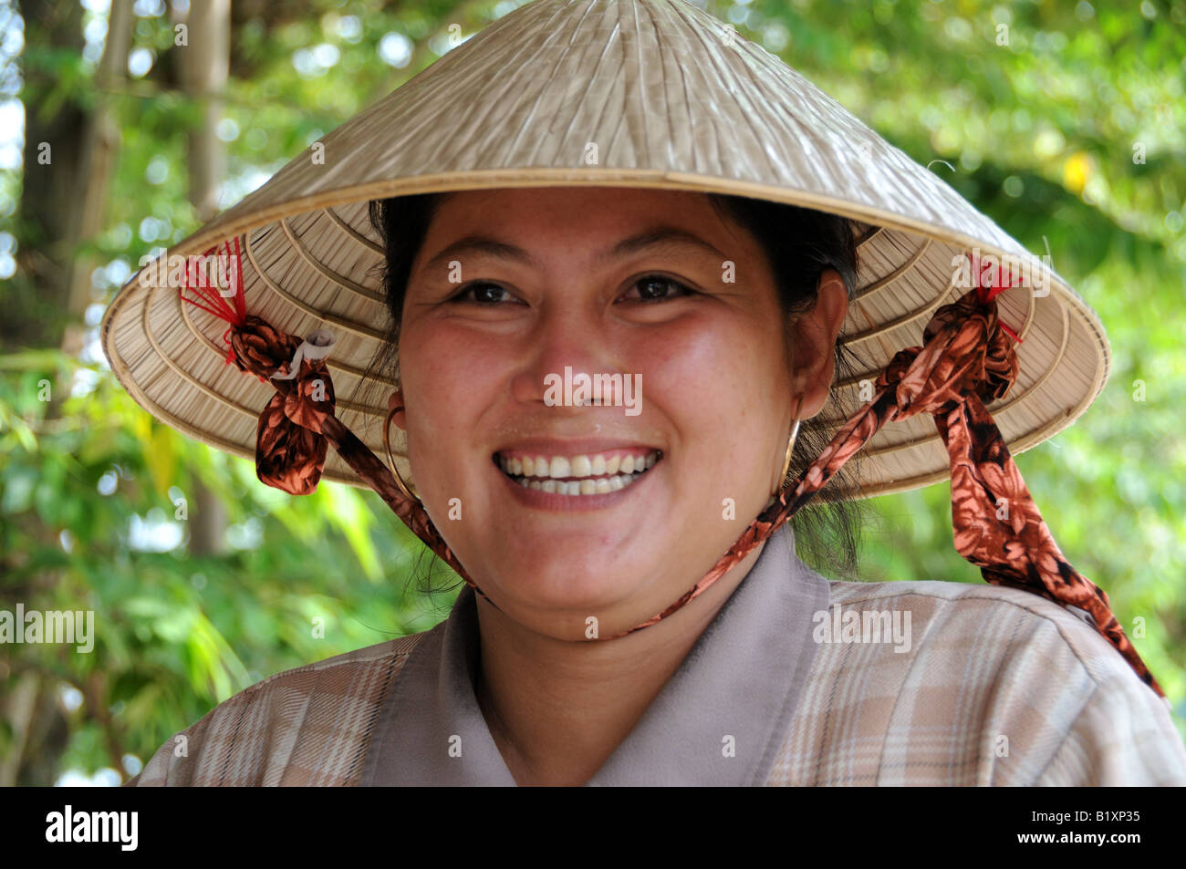Smiling face of a Vietnamese woman waring a traditional conical hat ...