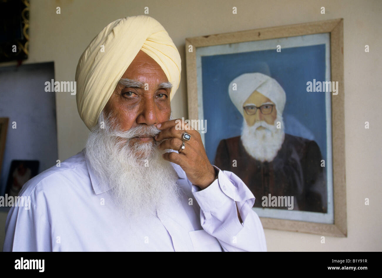 A turbaned Sikh stands in front of a painting of one of his relatives ...