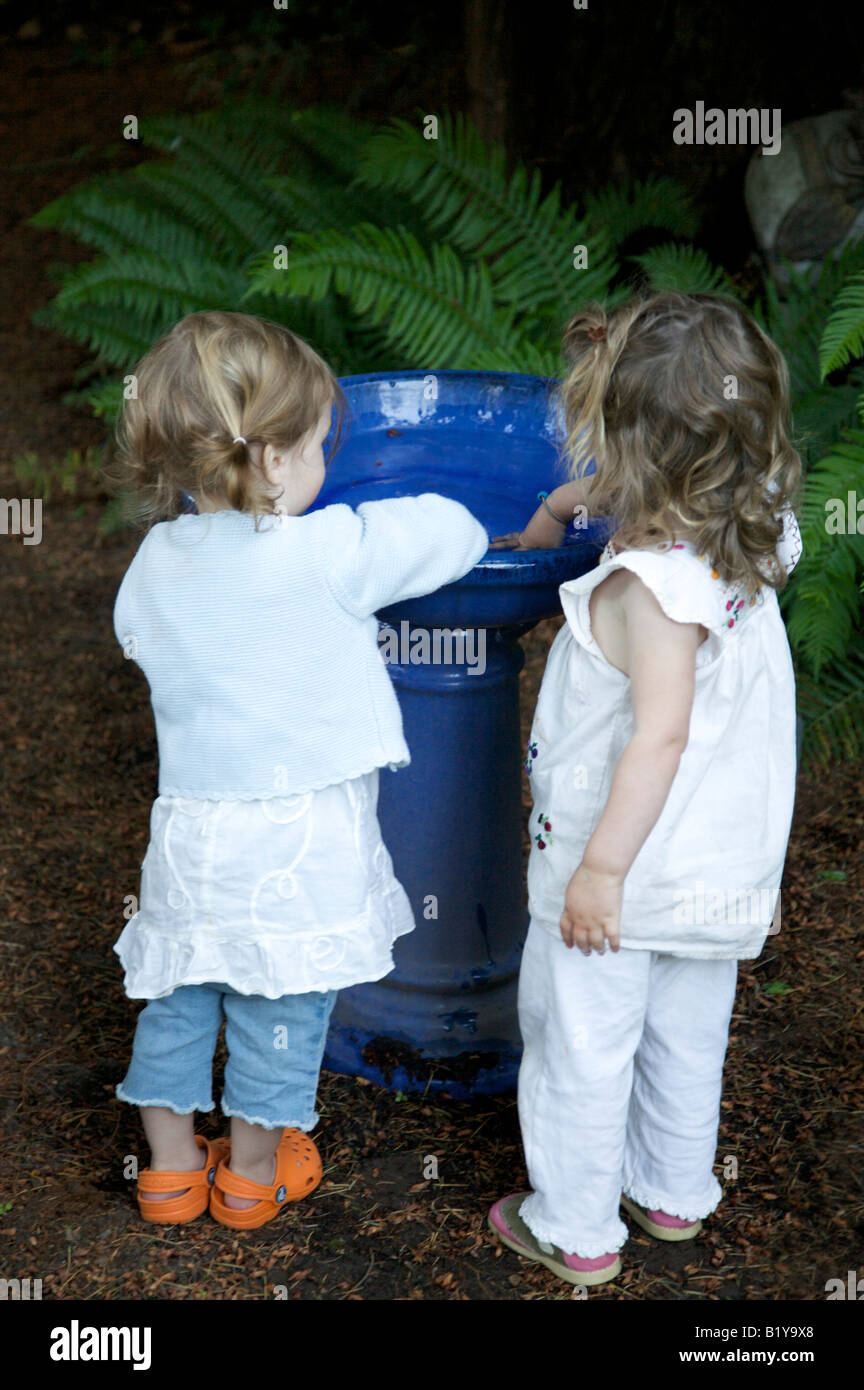 Two 20 month old girls swishing their hands the water of a blue ...