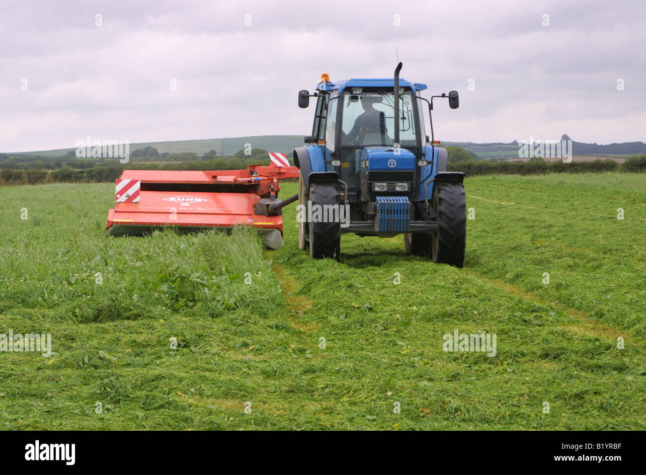 Blue Tractor and red farm machinery cutting grass for silage.Horizontal ...