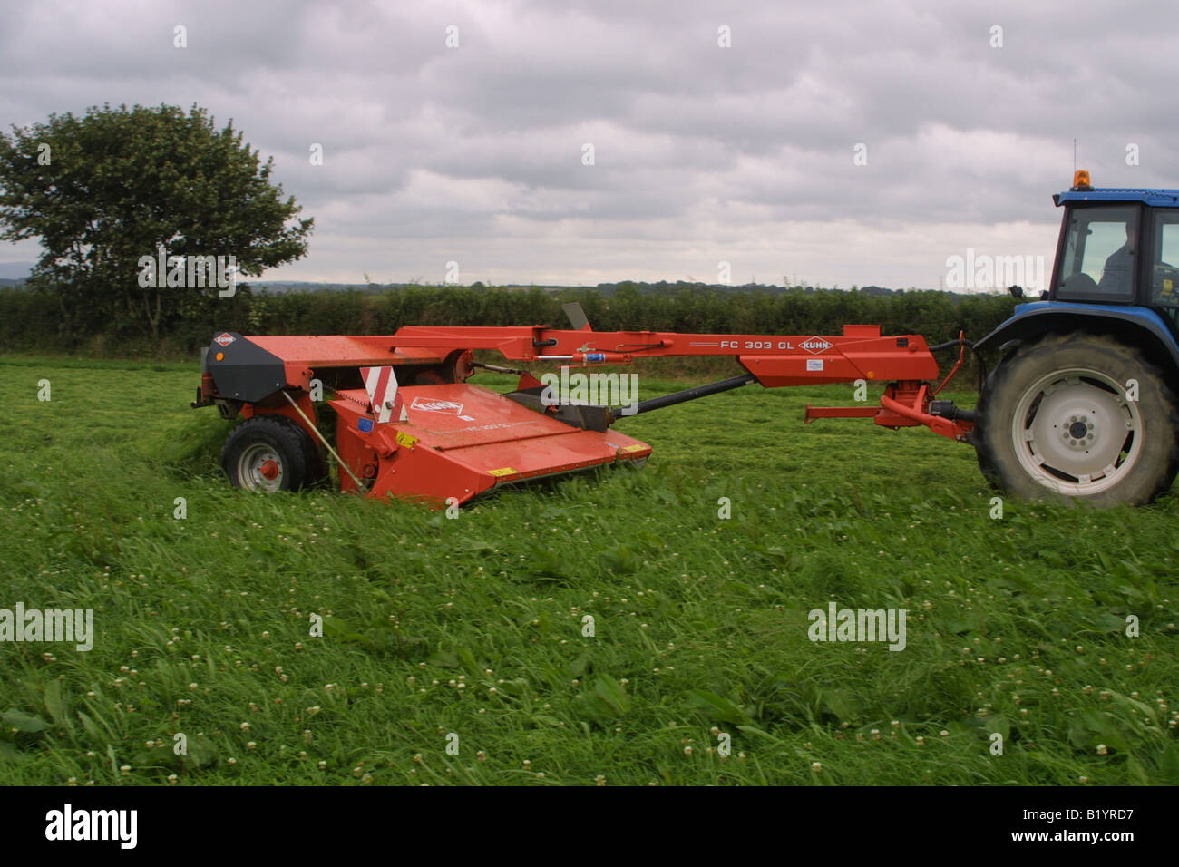 Tractor and red farm machinery cutting grass for silage.Horizontal ...