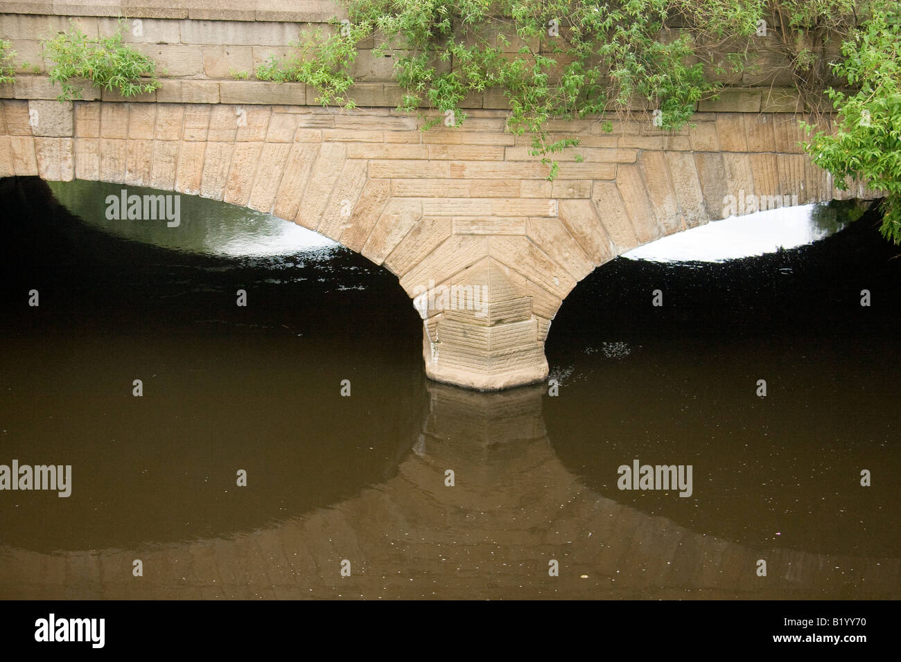 A stone bridge with plants and reflections over a muddy river Stock ...