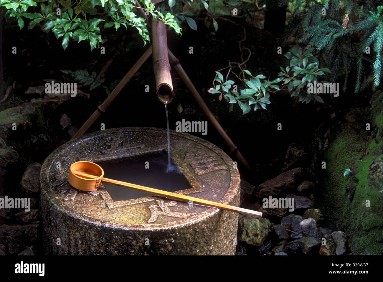 Bamboo ladle rests atop stone "tsukubai" water basin in the shape of an ...