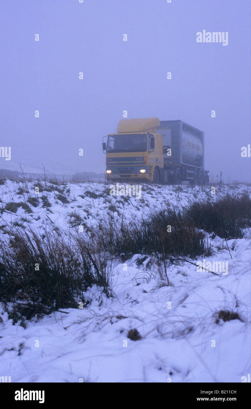 lorry travelling through fog and winter snow on moorland above ...