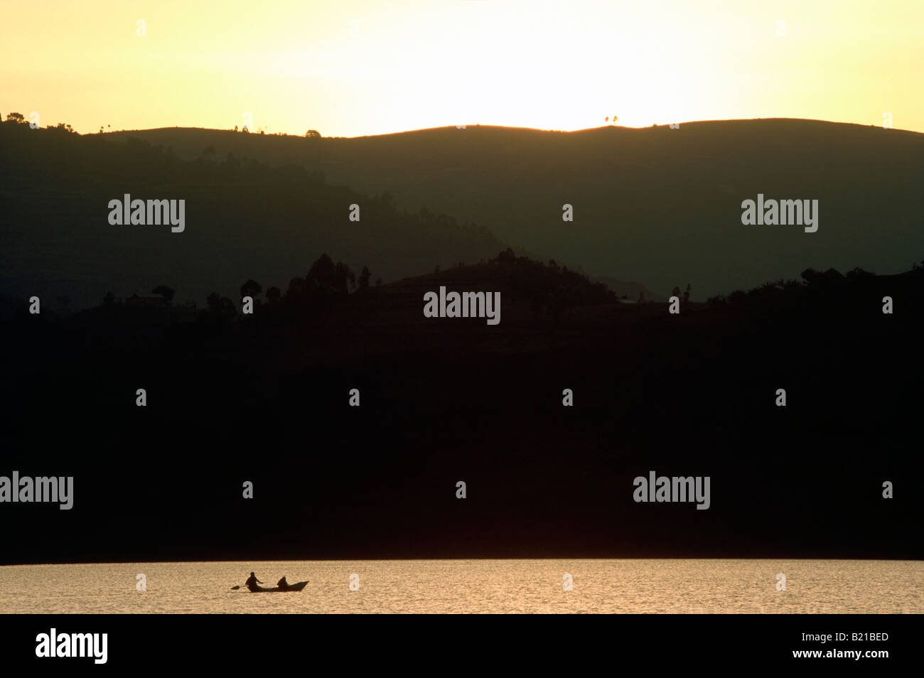 Two local men in a wooden dugout canoe paddeling across Lake Bunyonyi ...