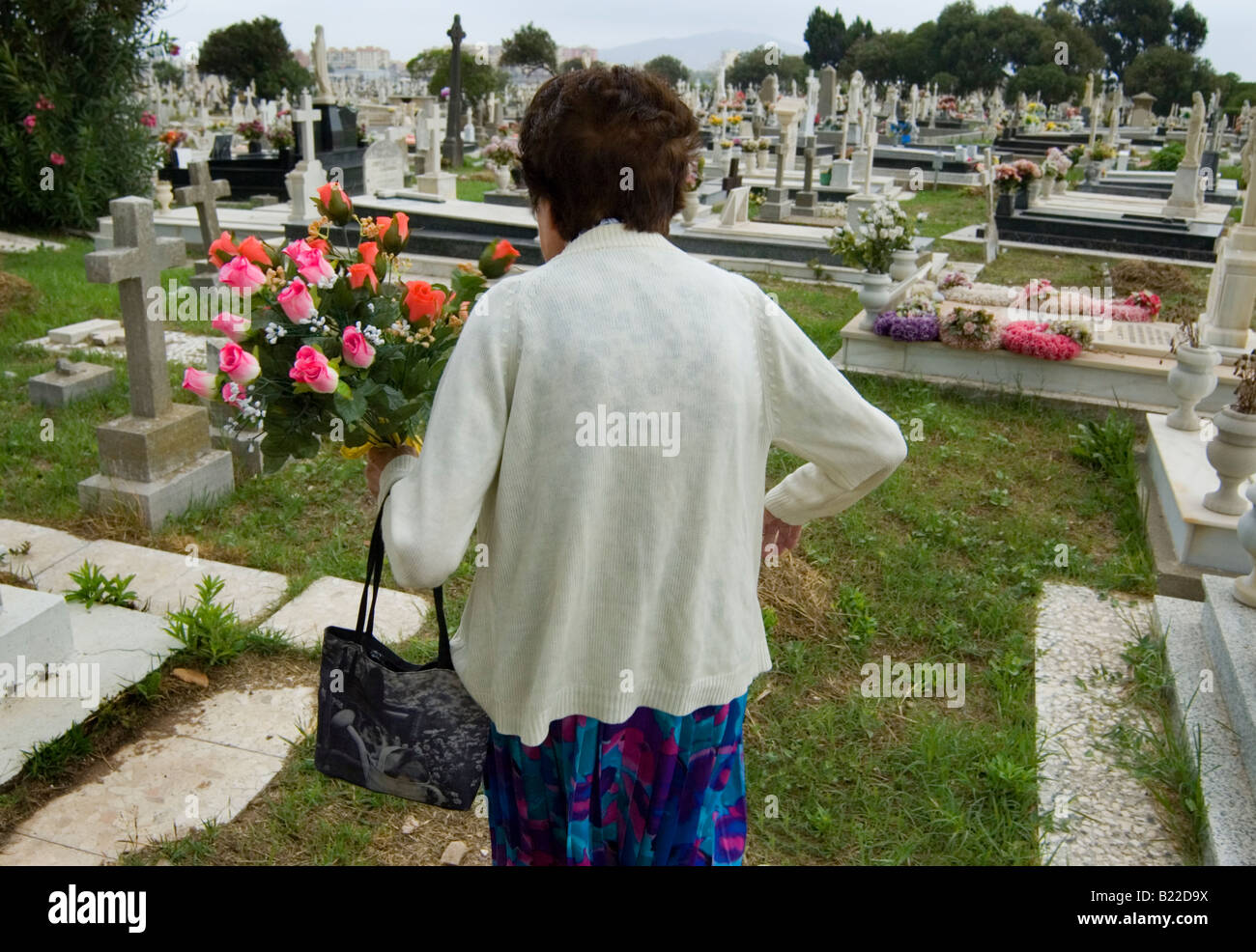An old woman walks through a cemetery with flowers in hand on way to ...