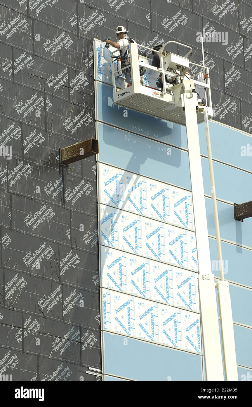 Workers on an elevated man lift install exterior panels over insulation ...
