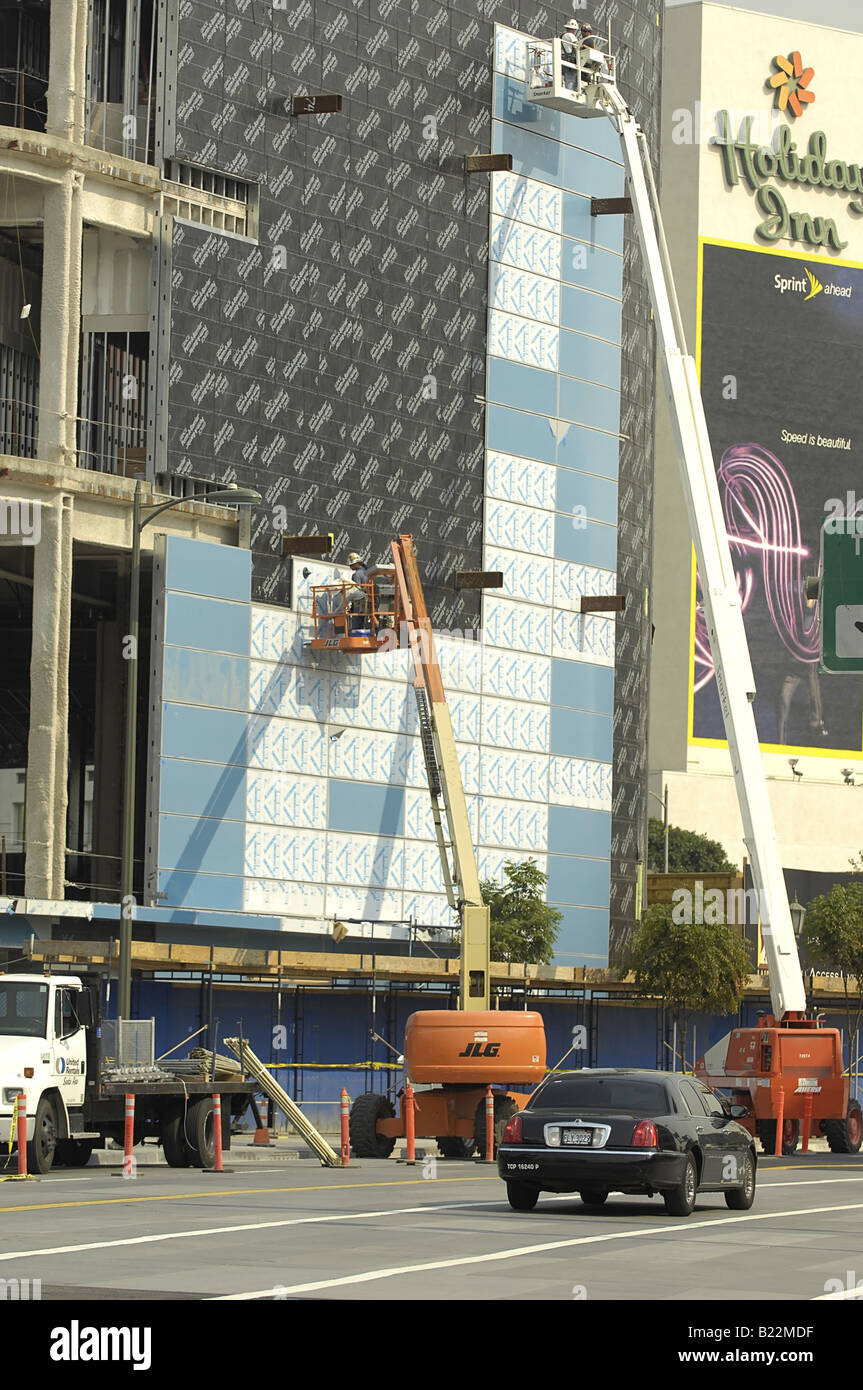 Workers on cherry picker cranes install insulation and other tiles on a ...
