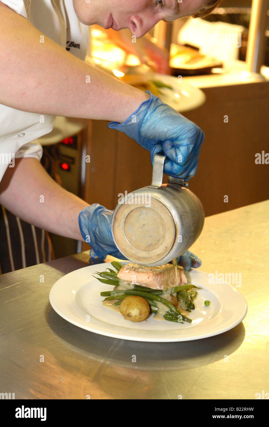Hotel restaurant kitchen staff plating up salmon fish dinner ready to ...