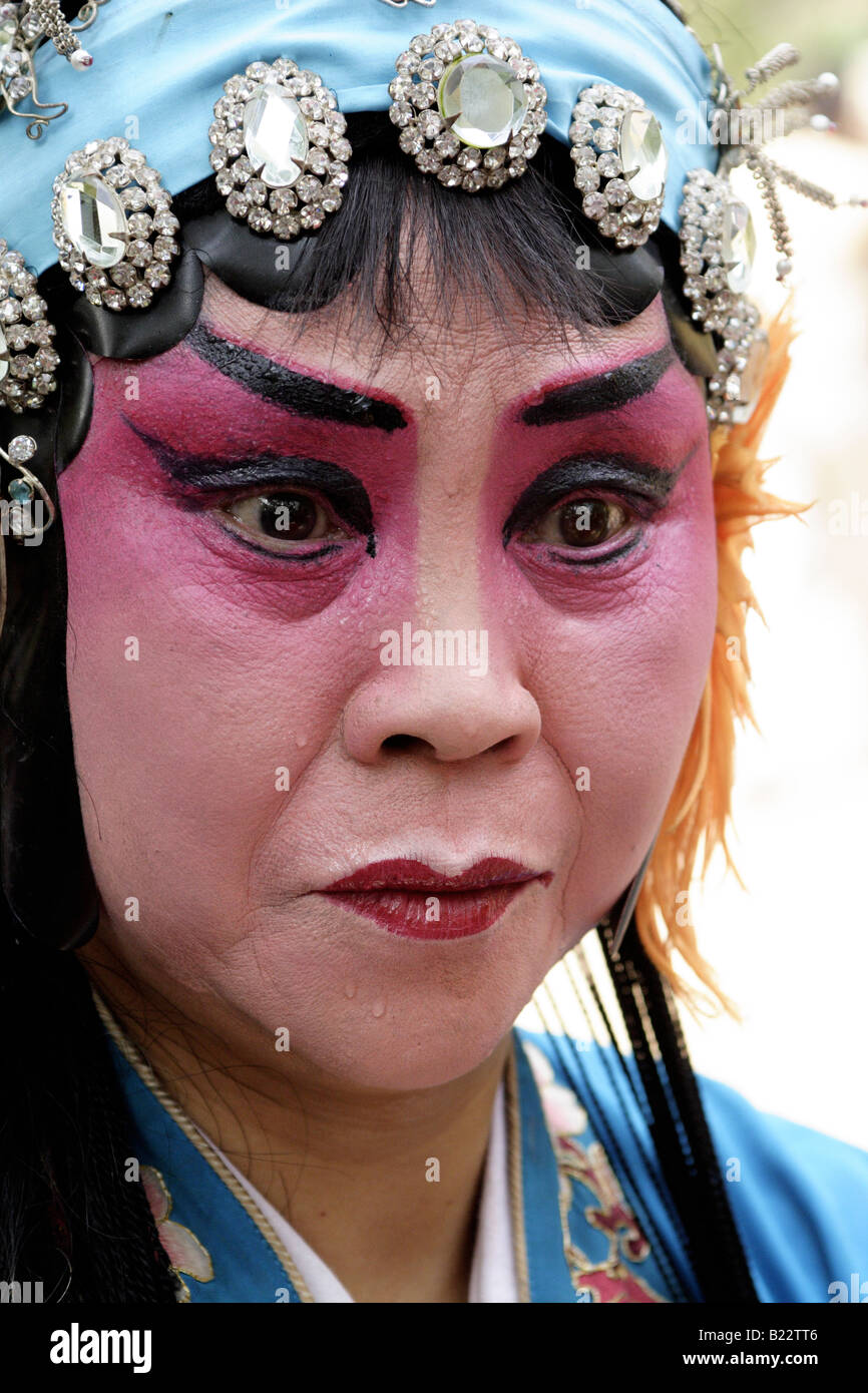 A female member of a Chinese opera company stands made up and ready to ...