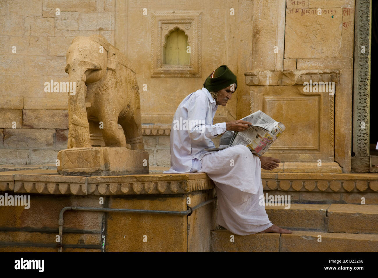 A man sits on a stone plinth in the street reading a newspaper ...
