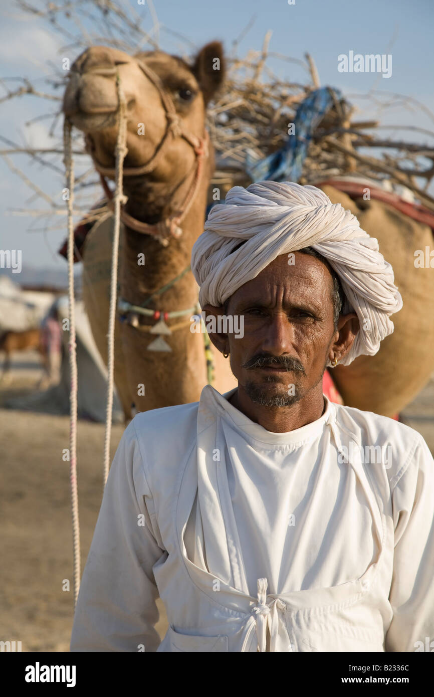 A male Rajasthani camel owner leading a camel loaded with firewood, at ...